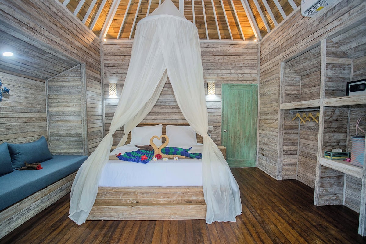 Um quarto de madeira com uma cama, um banco e um guarda-roupa.