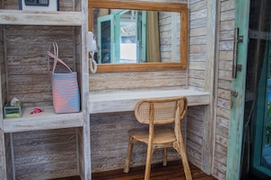 Um quarto rústico de madeira com uma estante contendo uma bolsa estampada, uma cadeira de vime e um espelho refletindo uma porta.