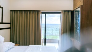 Quarto de hotel com cama, cortinas, televisão e vista para o mar.