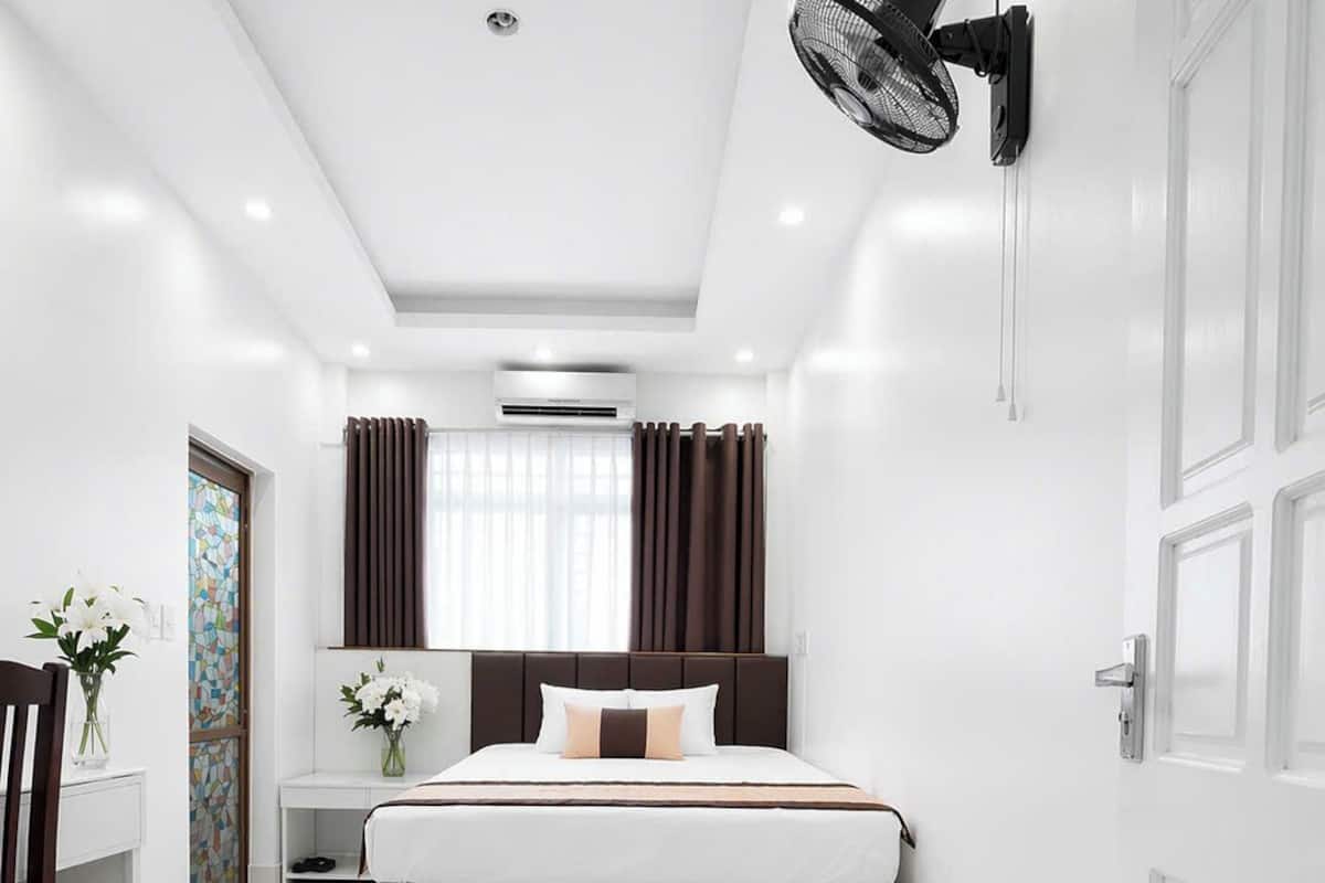 Um quarto moderno com cama, mesa de cabeceira e ventilador fixado na parede.