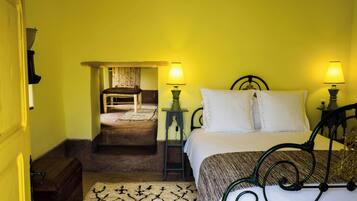 Quarto com cama, duas luminárias de cabeceira, um baú de madeira, um tapete estampado e uma escada que leva a uma pequena mesa com uma cadeira.