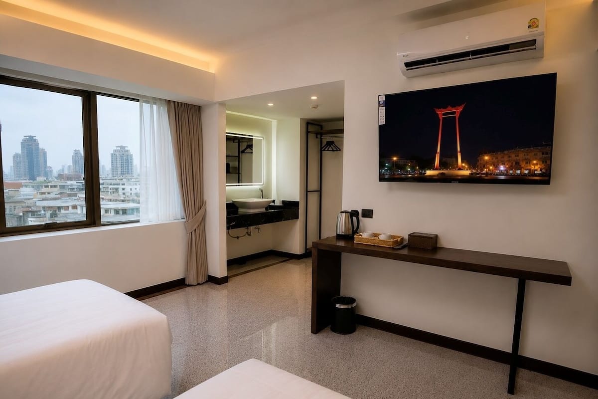 Quarto de hotel com duas camas, banheiro, escrivaninha com cafeteira e vista para a cidade.