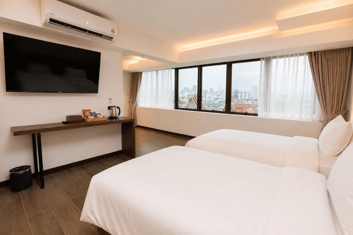 Quarto de hotel com uma cama, uma mesa com cafeteira, televisão e vista para a cidade.