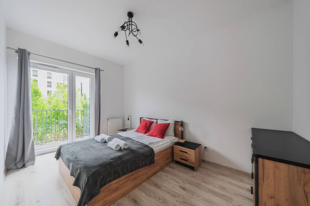 Quarto com cama, mesa de cabeceira, abajur e vista para o verde lá fora.