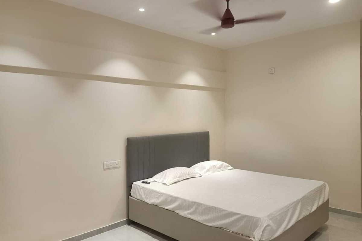 Quarto com cama, ventilador de teto, iluminação embutida e tomada na parede.