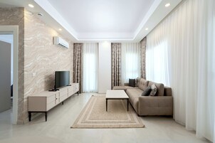 Uma sala de estar moderna com televisão de tela plana, um sofá bege, uma mesa de centro e um tapete estampado.