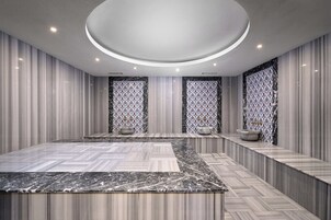 Um banheiro moderno com um amplo lavatório de mármore, uma luminária circular no teto e azulejos estampados.