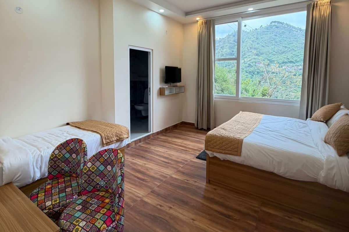 Quarto de hotel com duas camas, um ventilador de teto, televisão, janela com cortinas e uma cadeira estampada.
