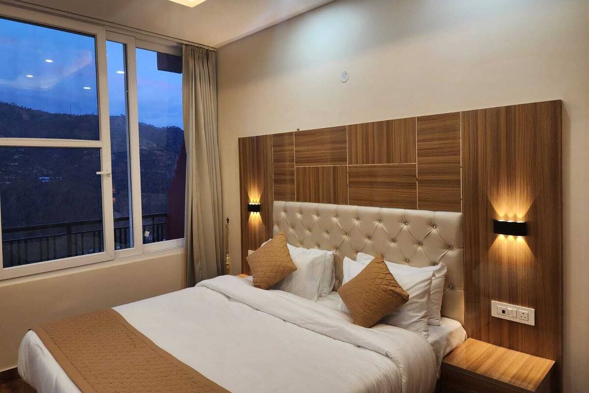 Quarto com uma grande janela, cabeceira estofada e luminárias laterais.
