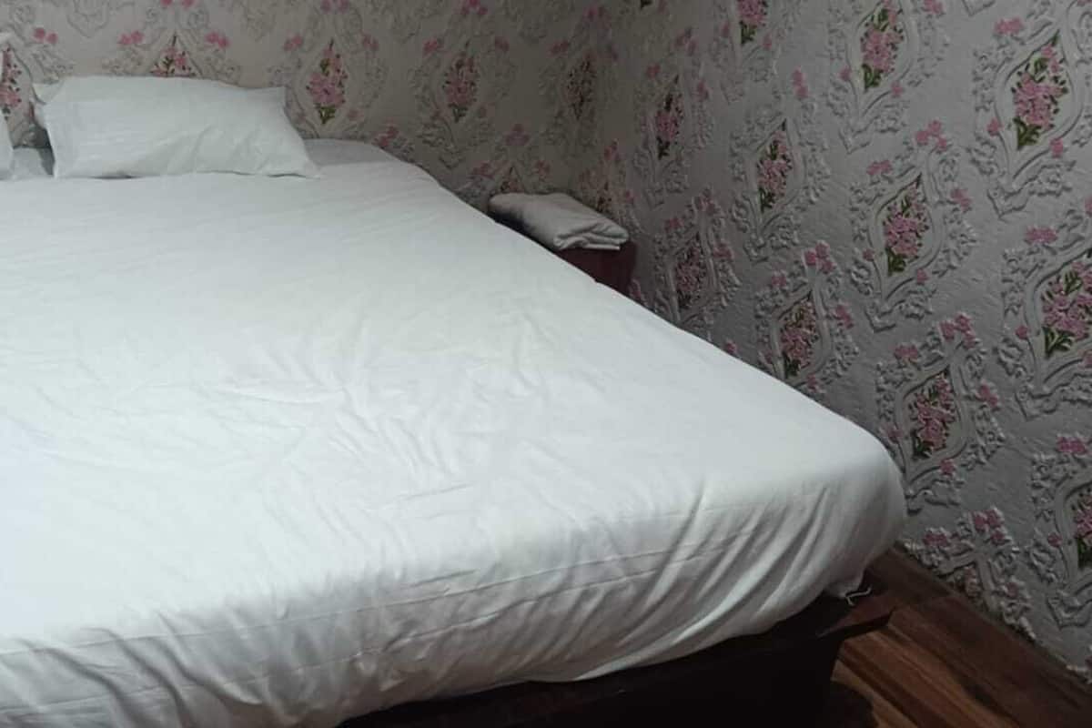 Uma cama com roupa de cama branca, um controle remoto e um telefone num criado-mudo.