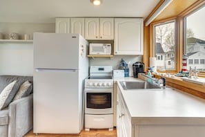 Cozinha compacta com geladeira, micro-ondas, forno e janela com vista para casas.