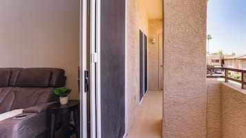 Varanda com vista para um edifício, porta de correr e um sofá marrom com uma planta.