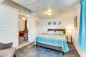 Quarto com cama, mesa de cabeceira, cadeira e porta que dá para outro cômodo.