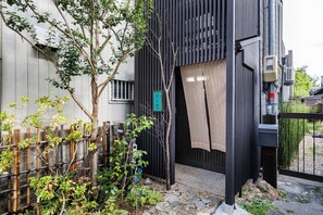 Um edifício com fachada escura, cerca de bambu e árvore de folhas verdes.