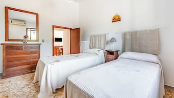 Quarto com duas camas, penteadeira de madeira, espelho, radiador e abajur.