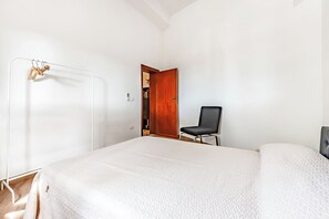 Quarto com cama, uma cadeira, guarda-roupa e porta que dá para outro cômodo.