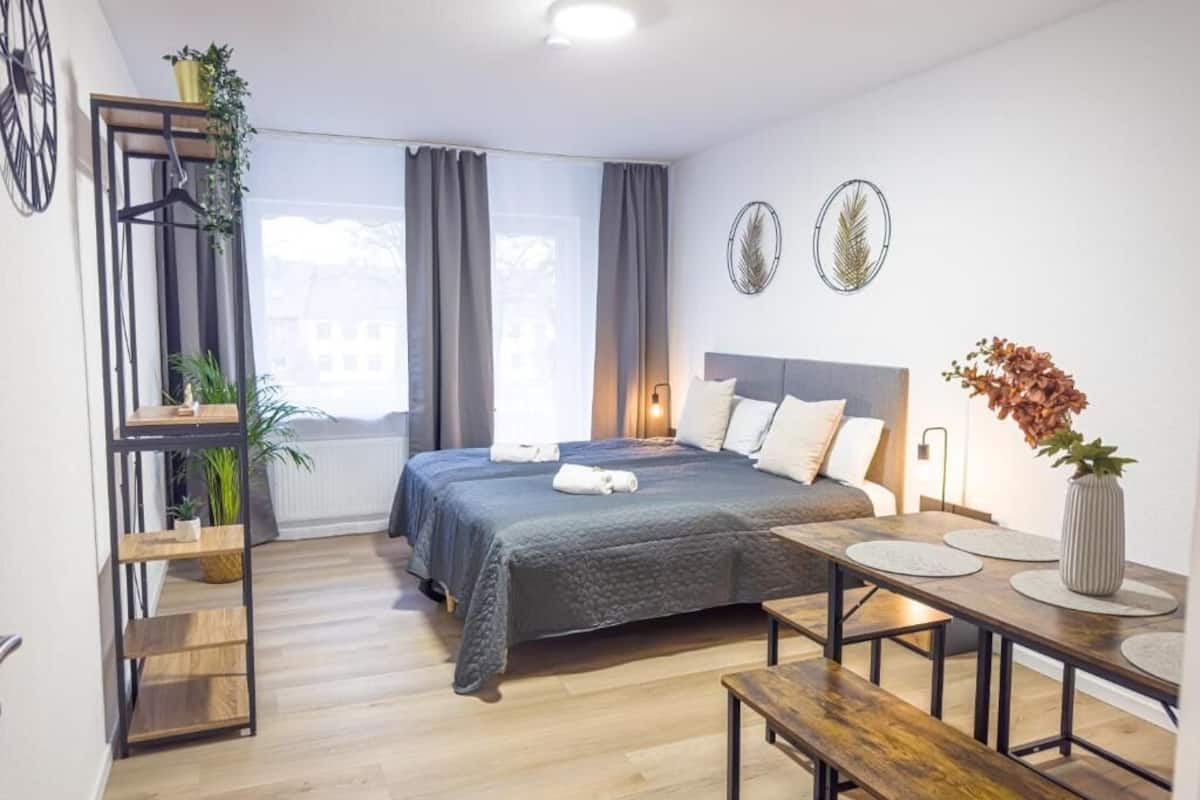 Quarto moderno com cama, mesa de cabeceira e janela com cortinas.