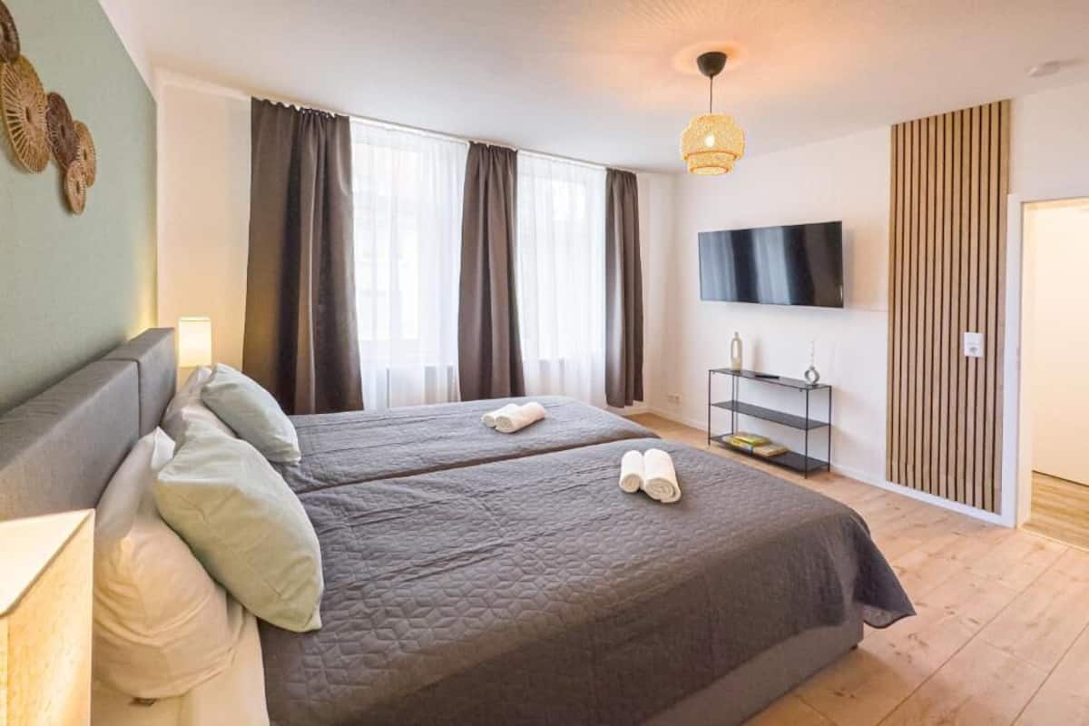 Quarto de hotel moderno com uma cama grande, televisão na parede e piso de madeira.