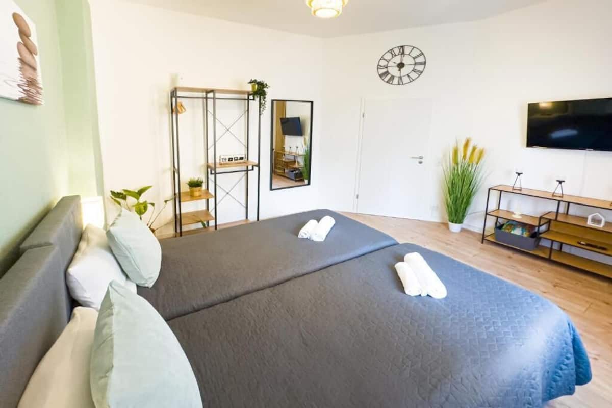 Um quarto moderno com uma cama grande, televisão, relógio e uma planta.