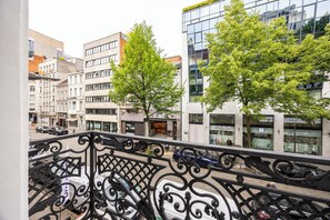Varanda com grades de ferro forjado, vista para uma rua com edifícios modernos e árvores.