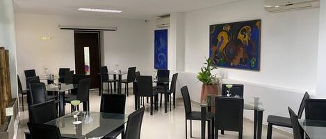 Uma sala de conferências com várias mesas e cadeiras, um quadro na parede e um aparelho de ar condicionado.