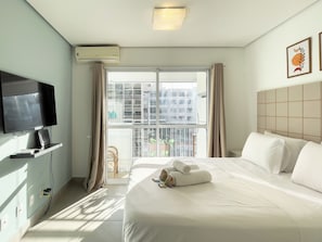 Quarto de hotel com cama, televisão, janela com cortinas e vista para prédios.