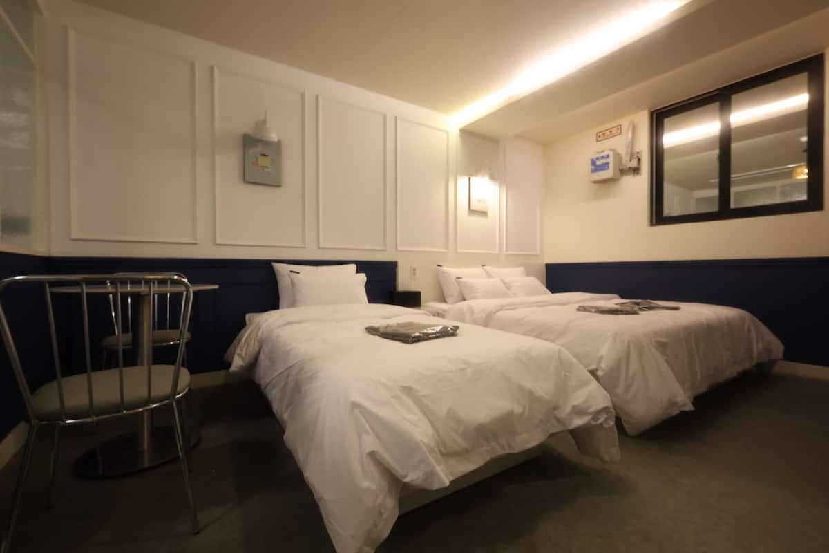 Quarto de hotel com duas camas, uma cadeira e uma janela.