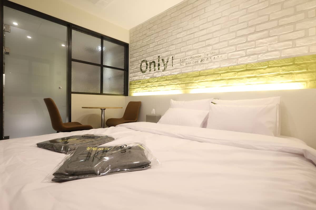 Quarto de hotel com cama, escrivaninha, cadeira e parede com padrão de tijolos.