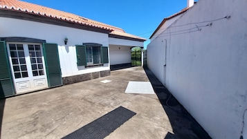 Uma viela estreita com um edifício branco com persianas verdes, telhado de telhas e chão de betão.