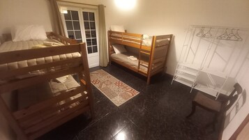 Quarto com duas camas beliche, uma escrivaninha pequena, uma cadeira, guarda-roupa com espelho e um tapete estampado.