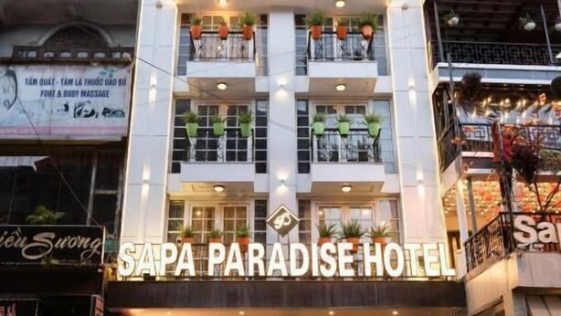 Um hotel com um letreiro que diz 'SAPA PARADISE HOTEL' e varandas com plantas em vasos.