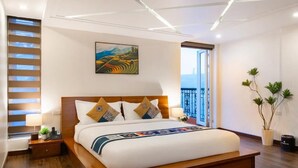 Quarto de hotel moderno com uma cama grande, um quadro na parede, uma janela com persianas e um vaso de planta.