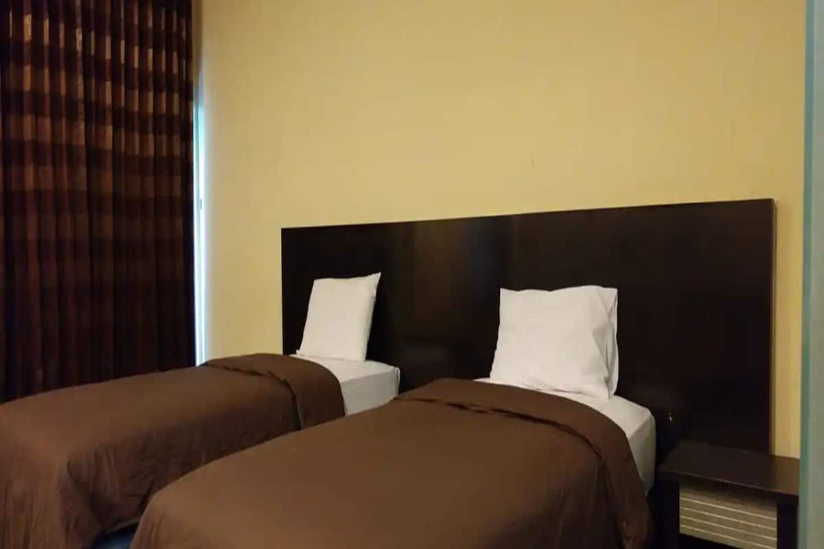Quarto de hotel com duas camas de solteiro, cada uma com colcha marrom e almofadas brancas, em frente a uma cabeceira escura.