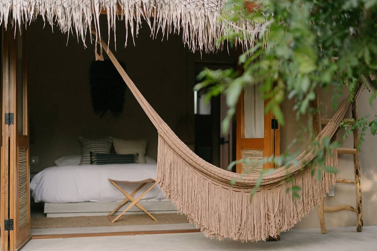 Uma rede em um quarto com uma cama, uma mesinha e uma escada de madeira.