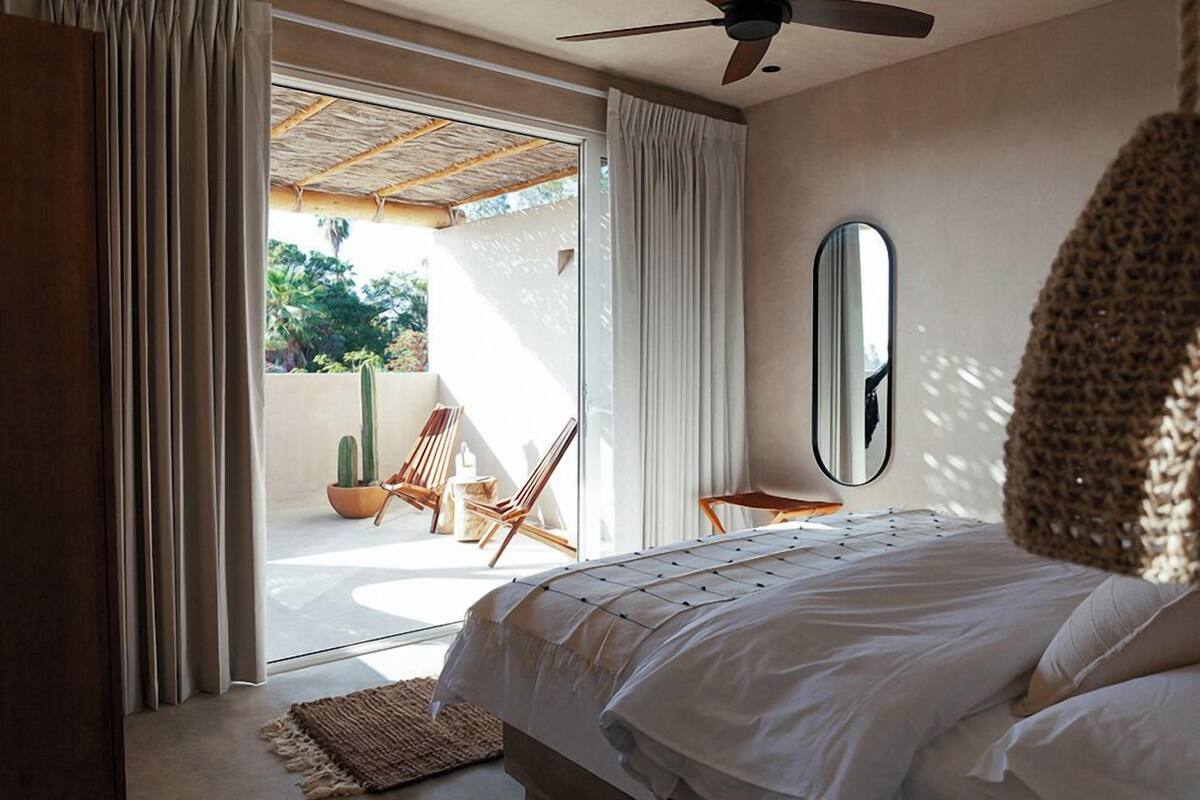 Quarto com cama, ventilador de teto, espelho grande e vista para o exterior.