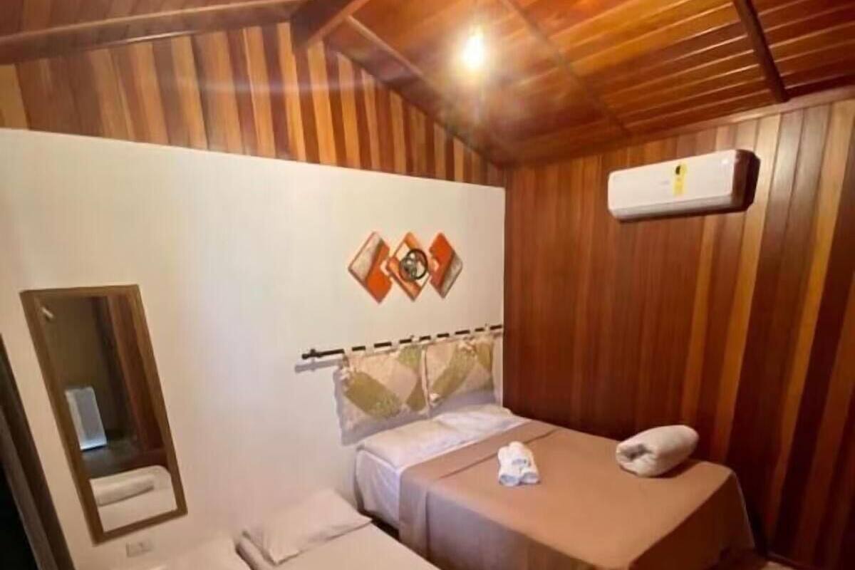 Quarto com duas camas de solteiro, uma pequena mesa, um espelho e ar-condicionado na parede.