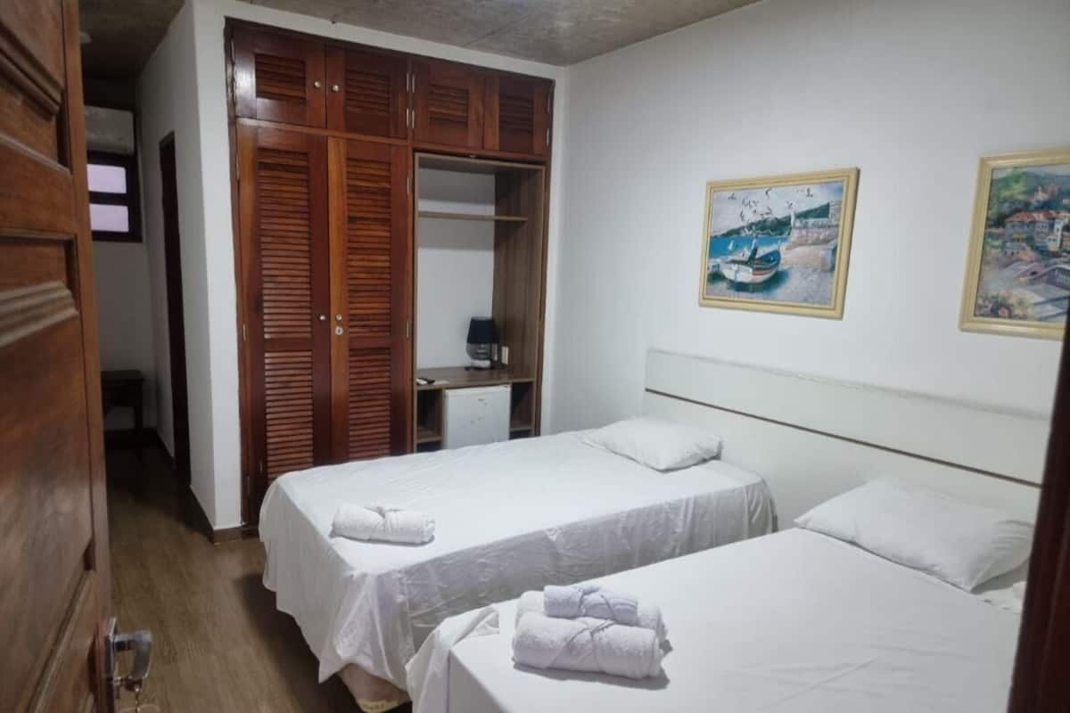 Quarto de hotel com duas camas, guarda-roupa de madeira e obras de arte na parede.