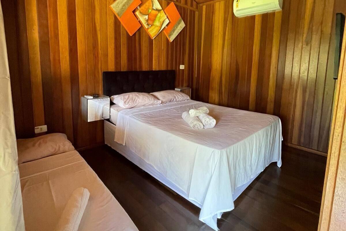 Quarto com painéis de madeira, uma cama, uma mesa de cabeceira e ar condicionado fixado na parede.