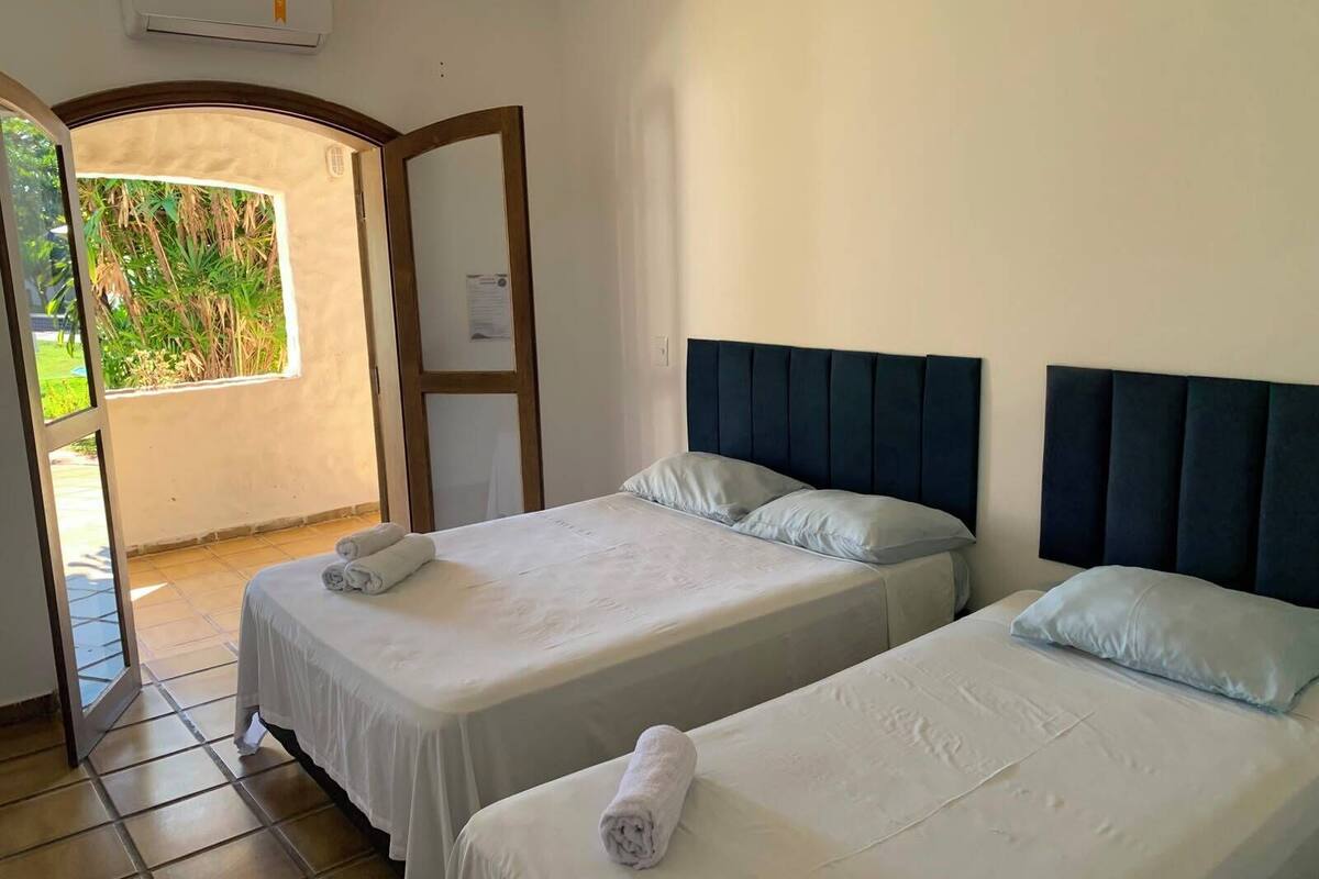 Quarto de hotel com duas camas, uma janela grande e uma porta para o exterior.