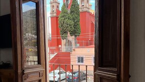 Quarto com porta de madeira que dá para área externa com um edifício vermelho, uma árvore e carros estacionados.