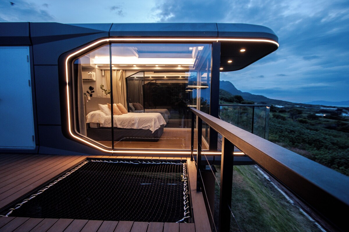 Quarto moderno com paredes de vidro, uma cama e vista para o exterior.
