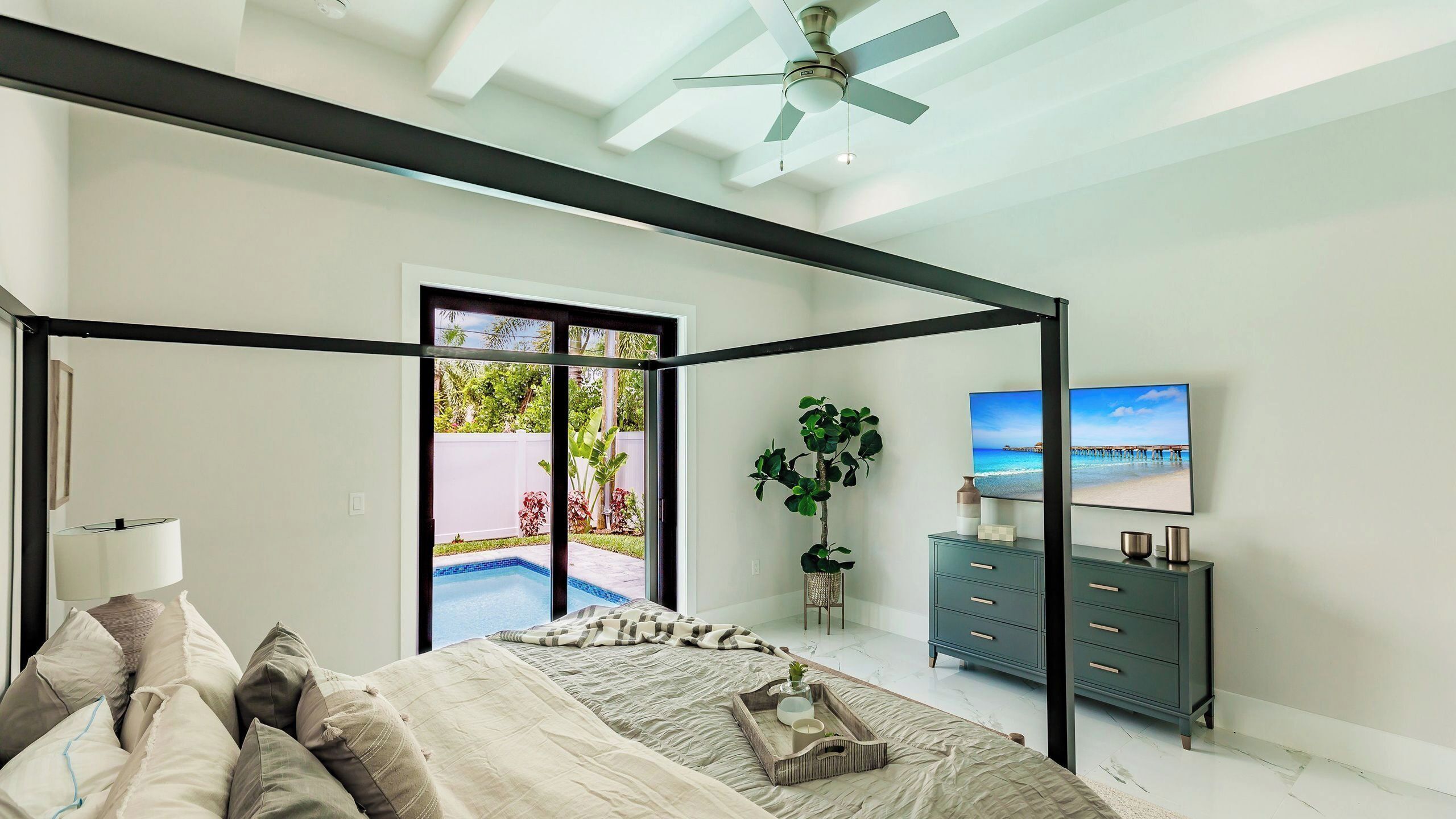 Quarto moderno com cama de dossel, televisão, cômoda e vista para uma piscina.
