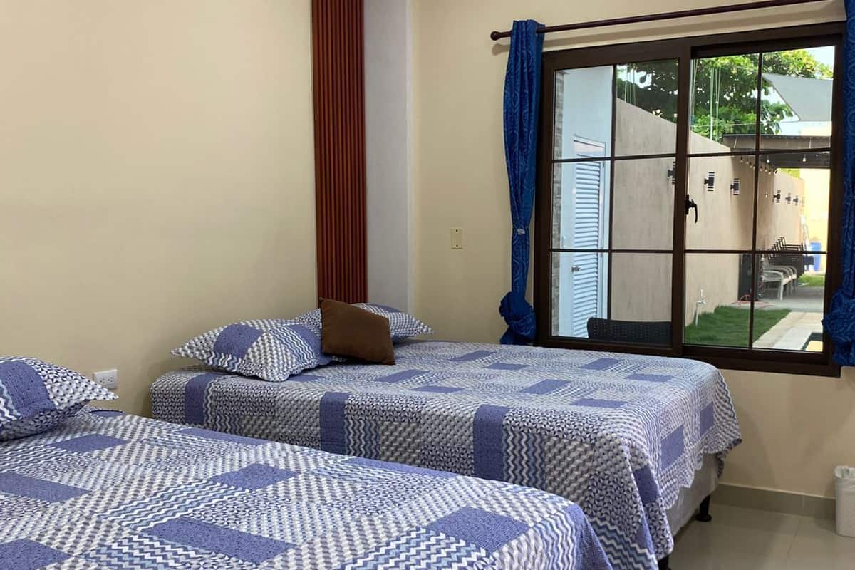Quarto com três camas, janela com cortinas e vista para o exterior.