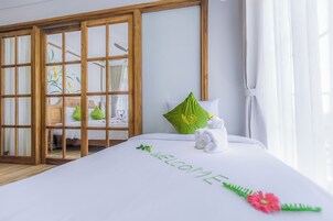 Quarto de hotel com uma cama, um travesseiro verde, uma toalha branca e uma placa de boas-vindas.