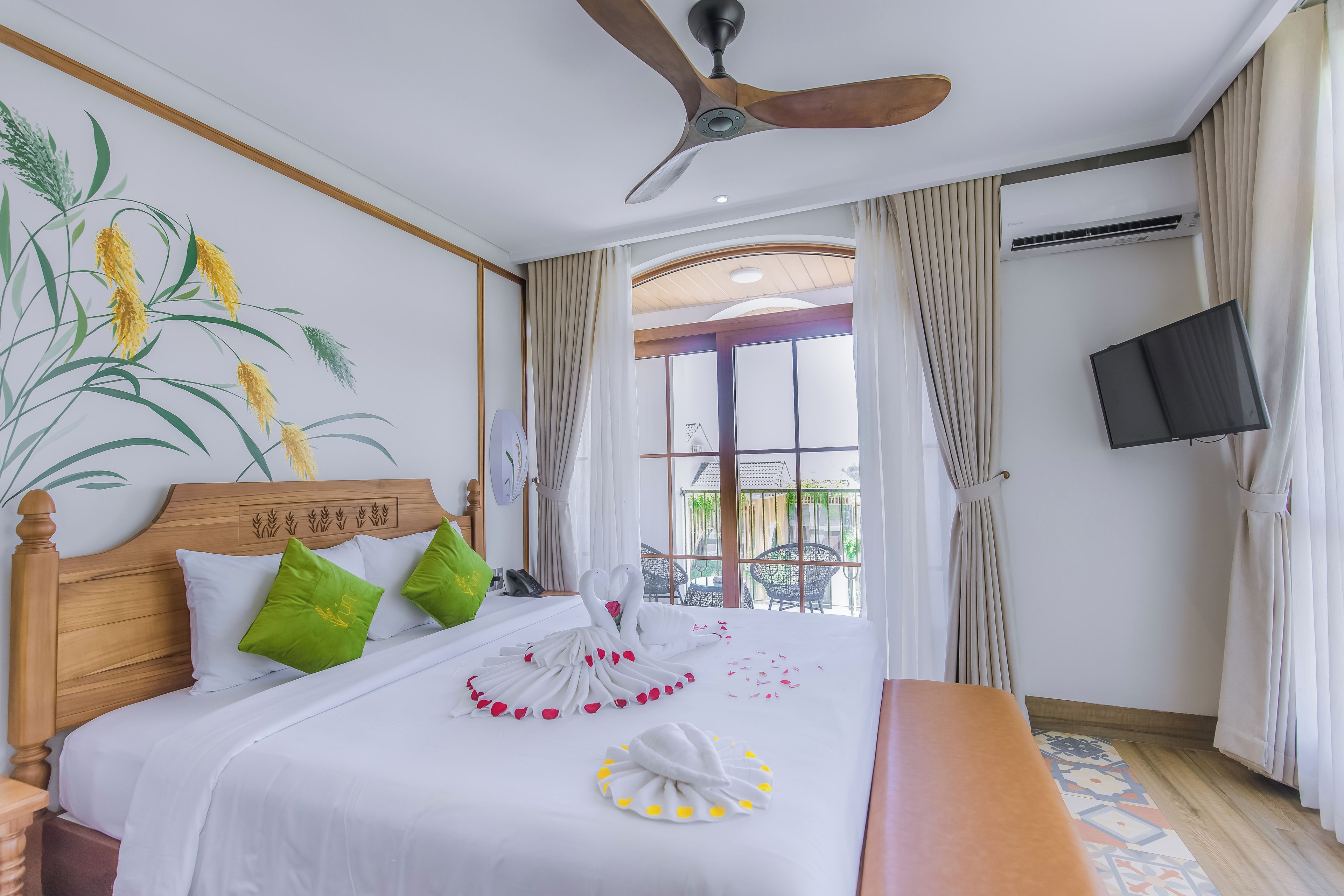 Quarto de hotel com cama, ventilador de teto, televisão e vista para o exterior.