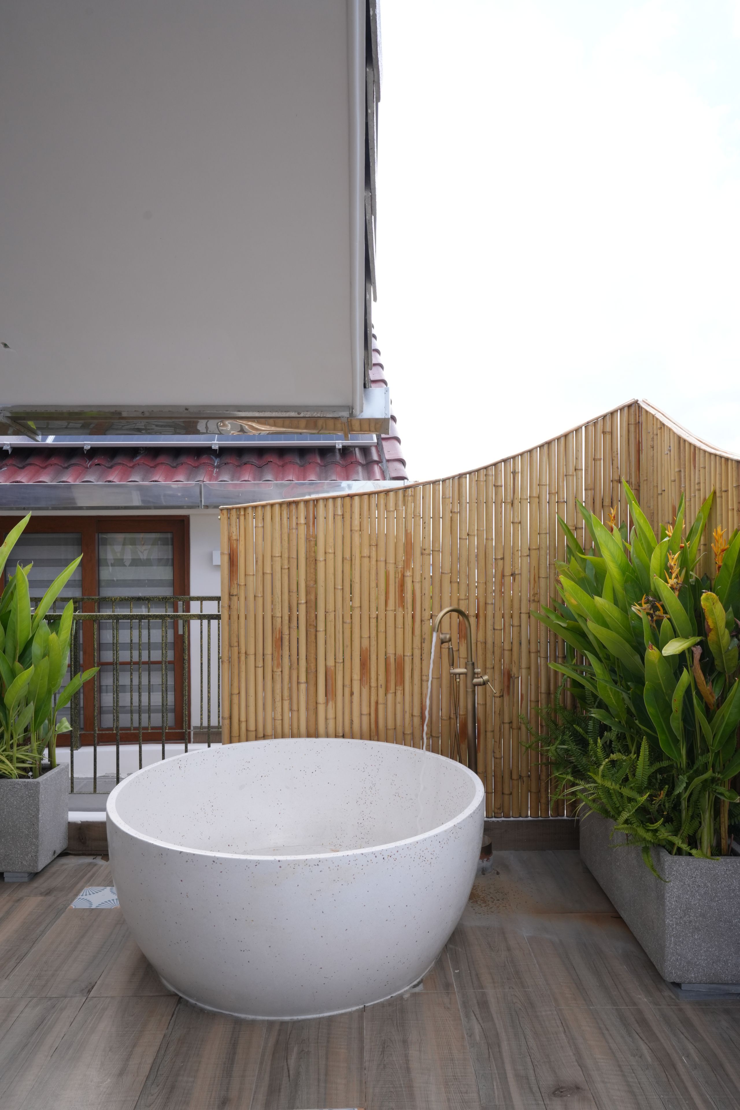 Uma grande banheira de hidromassagem ao ar livre em um deck de madeira, com cercado de bambu e plantas em vasos.