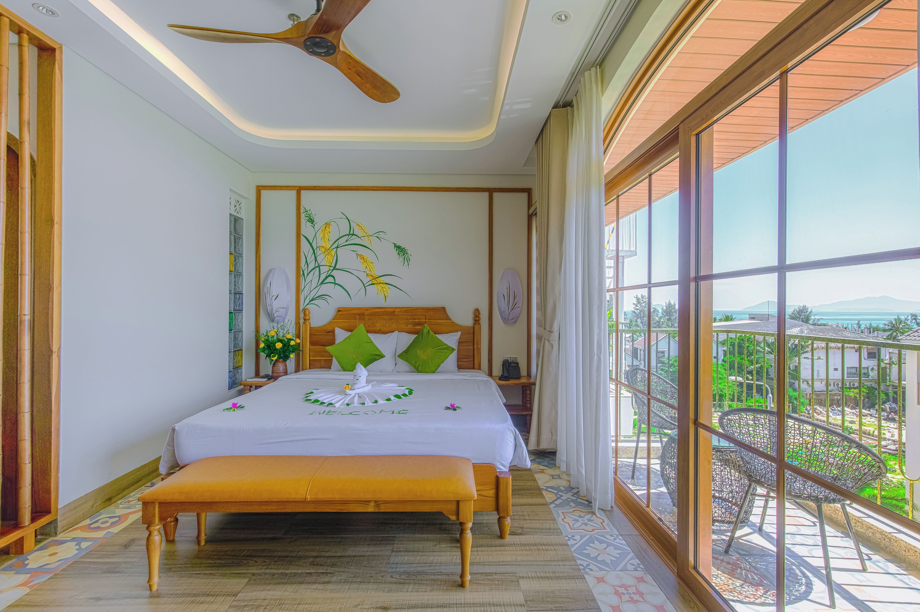 Quarto com cama grande, um banco de madeira, ventilador de teto e vista para o exterior.