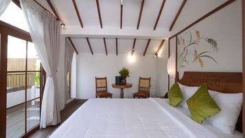 Quarto com uma cama grande, cabeceira de madeira, duas cadeiras, uma mesa pequena com um vaso e uma varanda com vista.