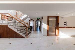Um hall amplo com piso de mármore, escada de madeira e elevador.