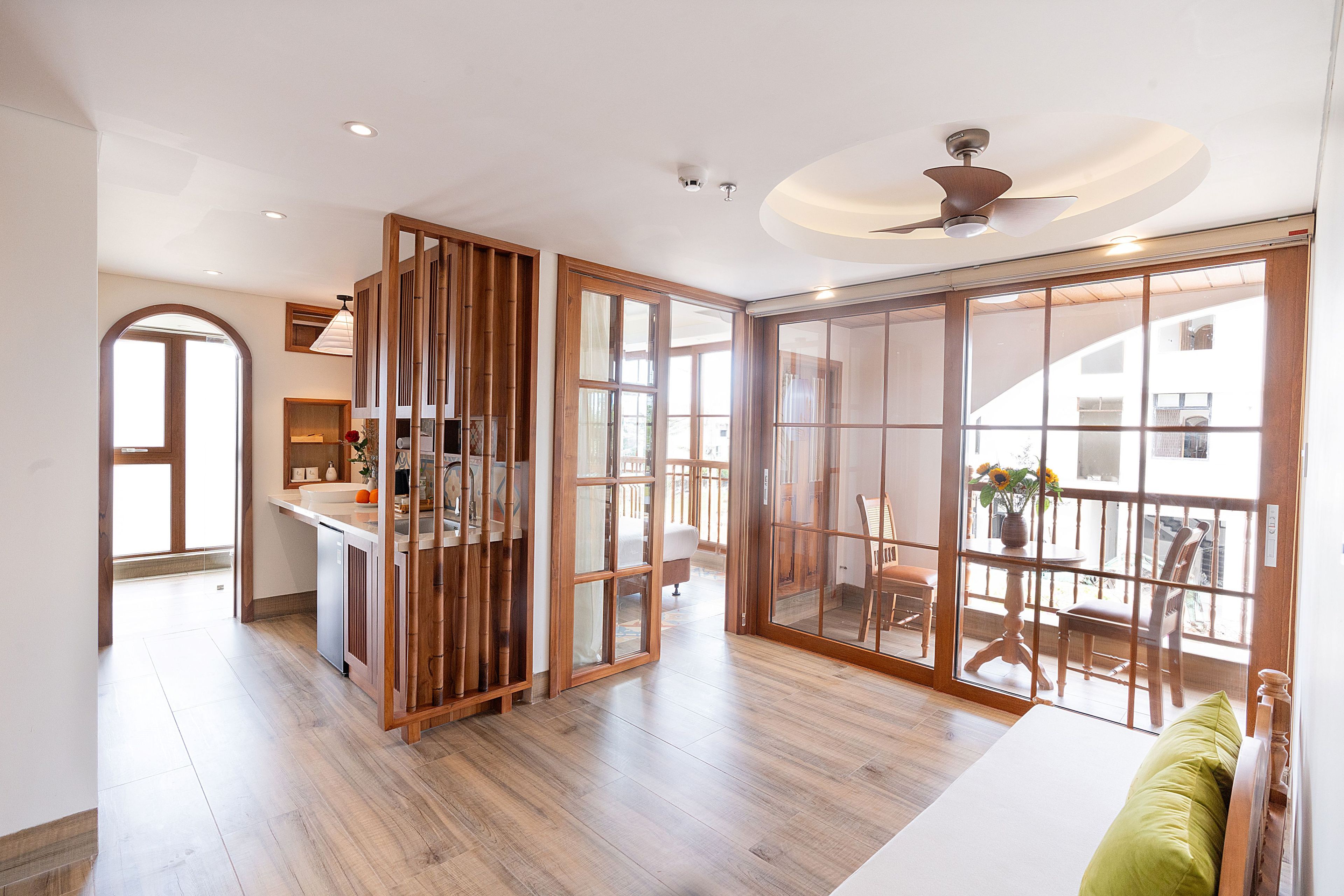 Um quarto amplo com piso de madeira, área de refeições com mesa e cadeiras, e uma grande porta de vidro deslizante que dá para uma área externa.